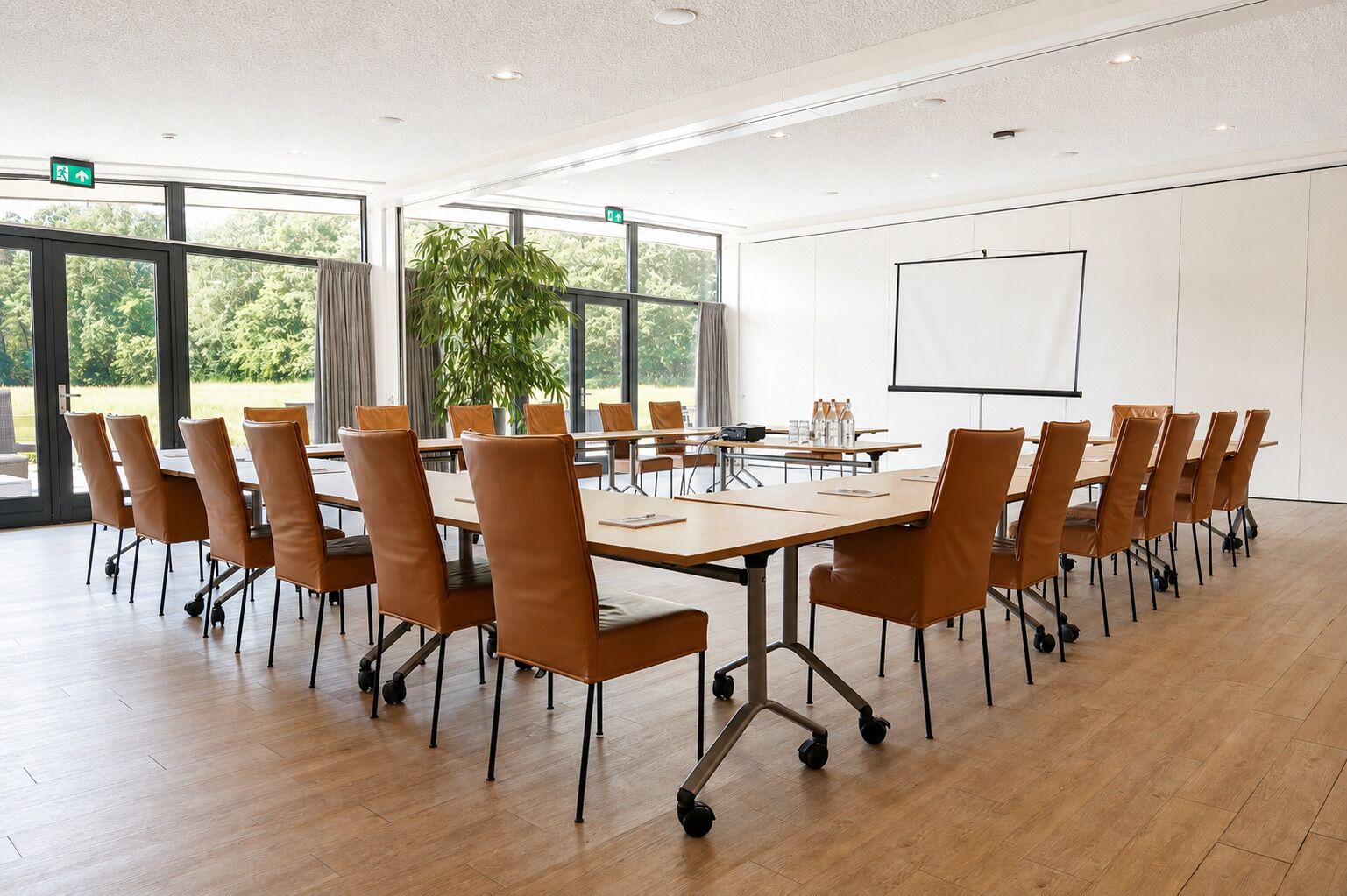 Uma sala de conferências com uma mesa comprida, cadeiras, uma tela de projetor e janelas amplas.