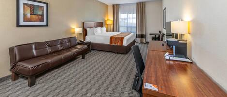 Quarto de hotel com uma cama, um sofá de couro castanho, uma escrivaninha de madeira e uma televisão.