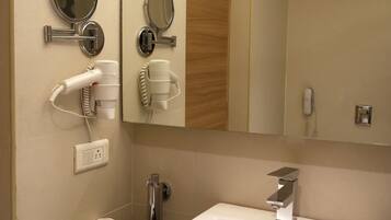 Casa de banho moderna com uma pia branca, dois espelhos fixados na parede, um secador de cabelo e um telefone.