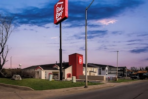 Um Red Roof Inn com uma placa vermelha grande, um estacionamento e um edifício com telhado plano.