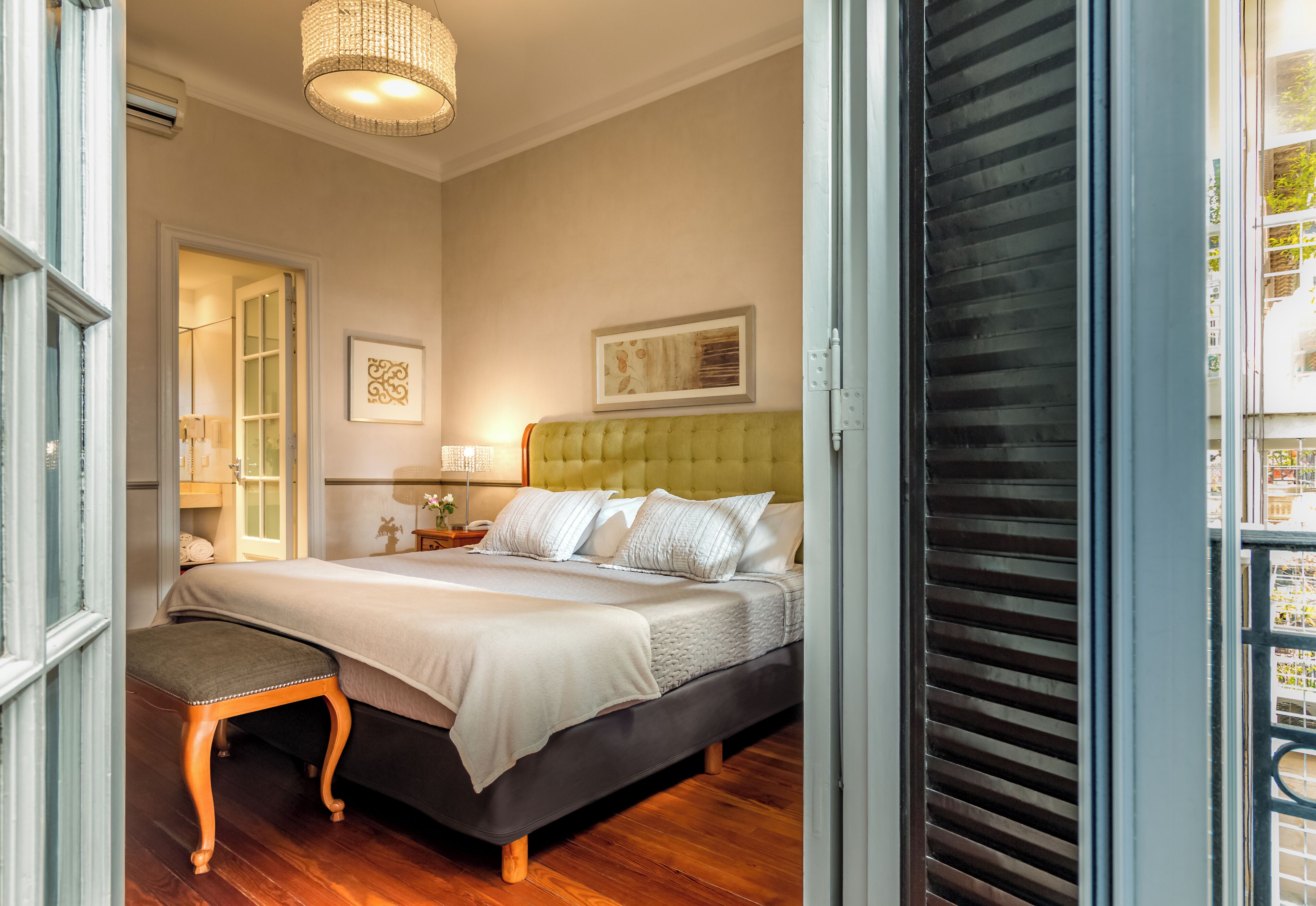 Quarto com cama, mesas de cabeceira, abajur, cadeira e janela com persianas.