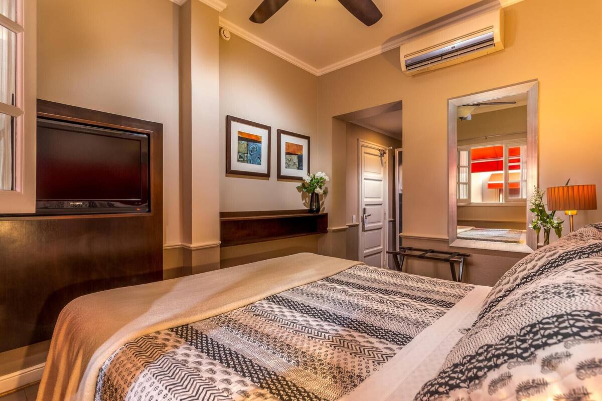 Quarto de hotel com cama, televisão, obras de arte emolduradas, porta e janela com cortinas.