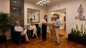 Um lobby de hotel com piso em padrão herringbone, um espelho grande e um candelabro.