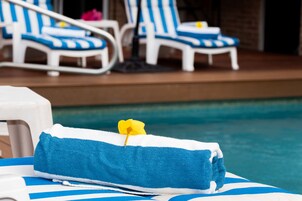 Área da piscina com espreguiçadeiras e uma toalha com uma flor amarela.