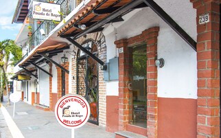 Hotel chamado 'Hotel Posada de Roger', com uma placa de 'Boas-vindas', fachada de tijolos e o número '239' visível.