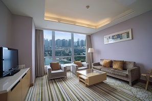 Quarto de hotel moderno com uma janela ampla que oferece vista para a cidade, uma TV de tela plana, um sofá, uma mesa de centro e um abajur.