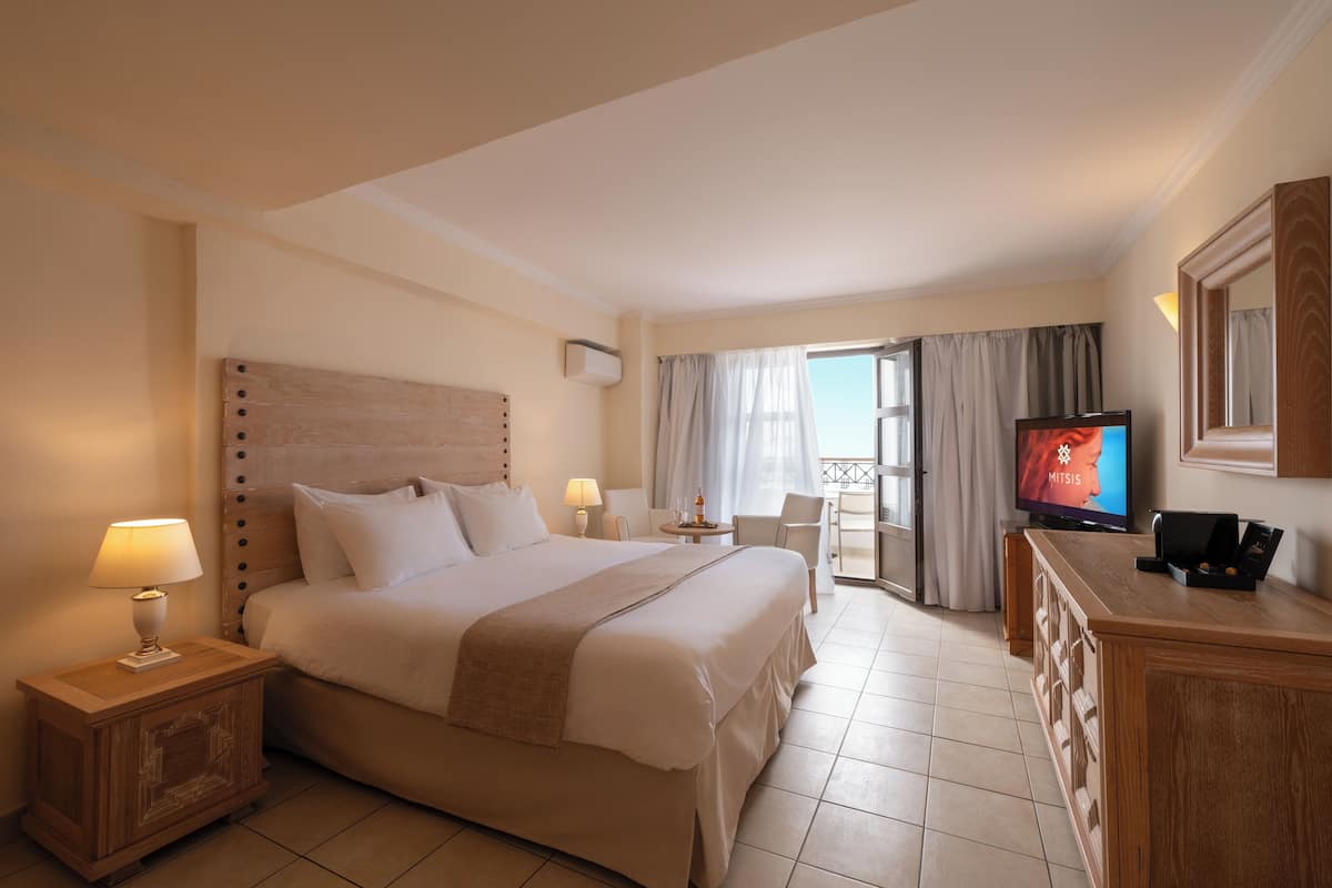 Quarto de hotel com uma cama grande, luminárias de cabeceira, televisão, escrivaninha e vista para o exterior.
