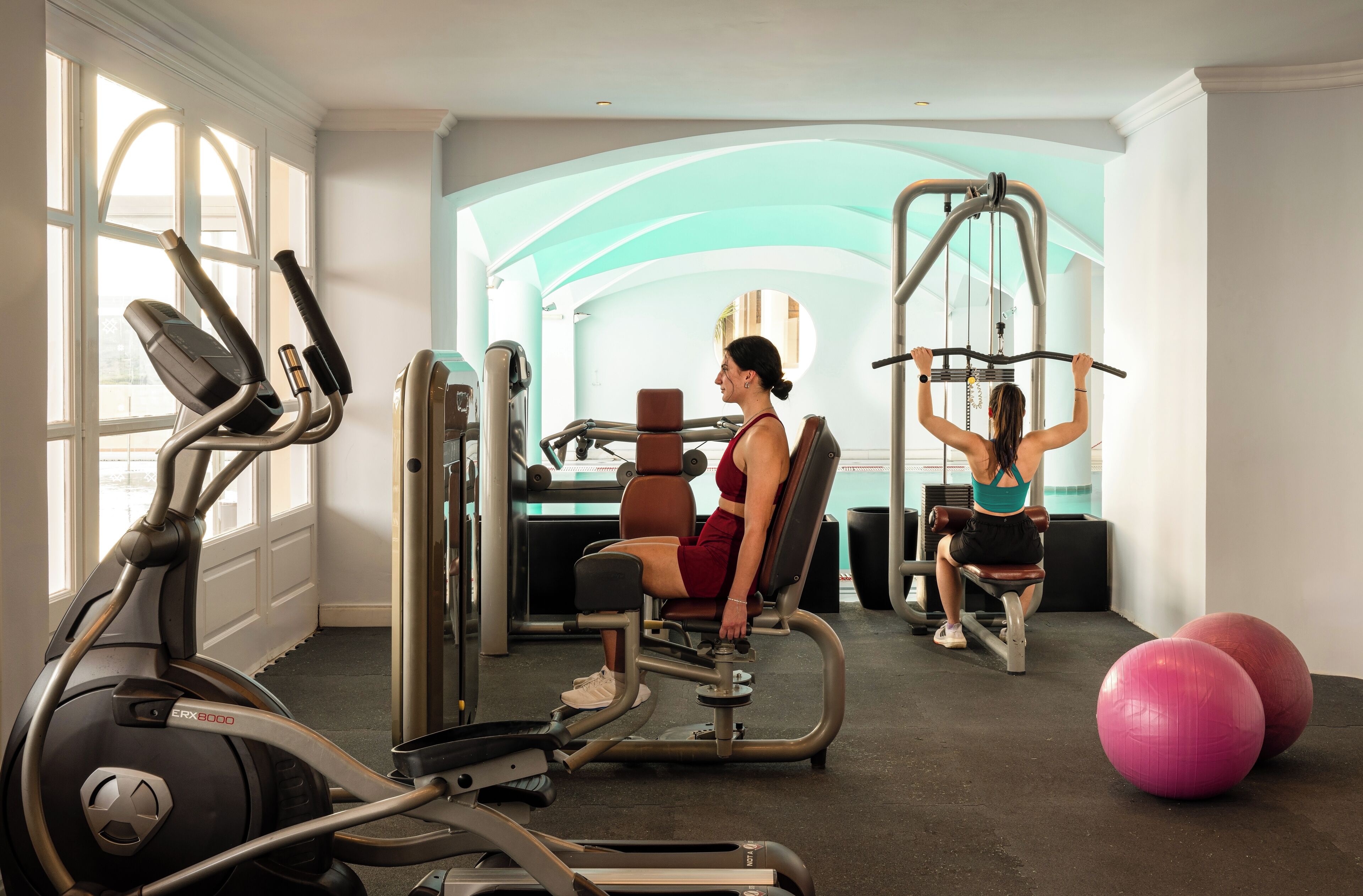 Uma academia com equipamentos de ginástica, uma elíptica para uso sentado e bolas de exercício grandes.