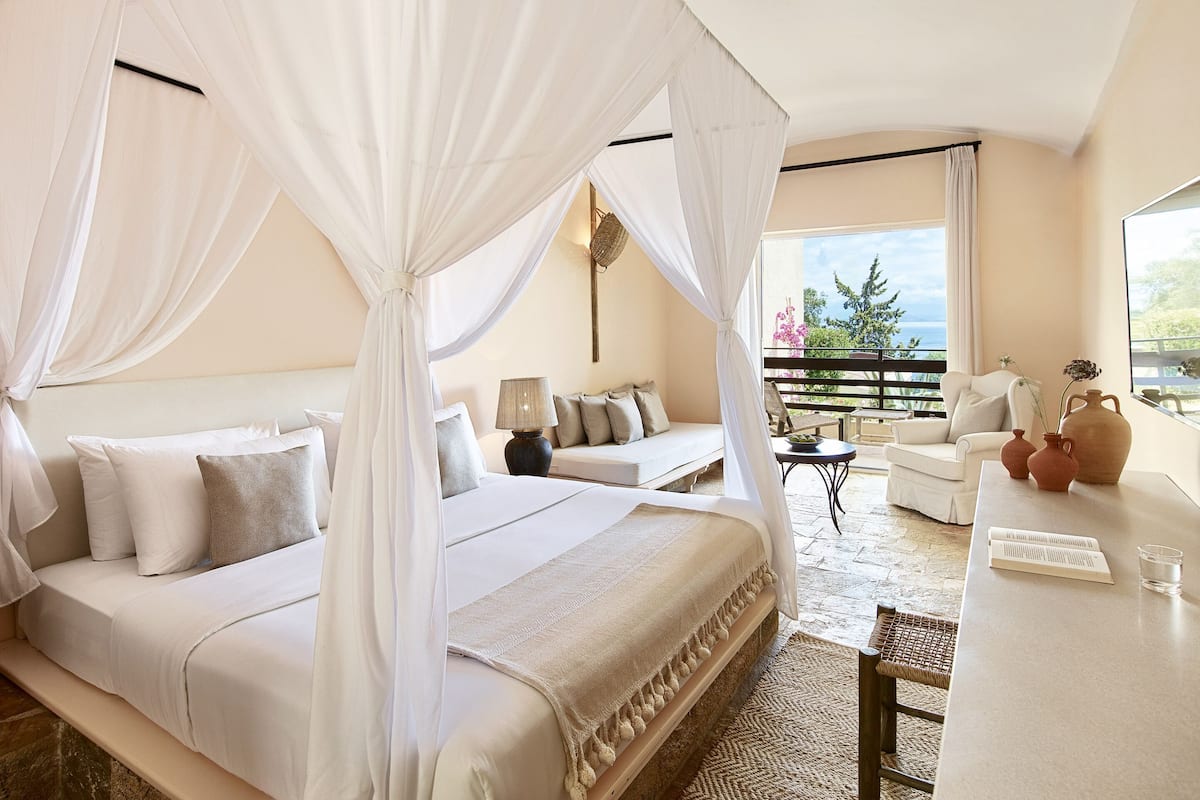 Quarto com cama de dossel, um sofá, uma mesa com vasos e vista para o exterior.
