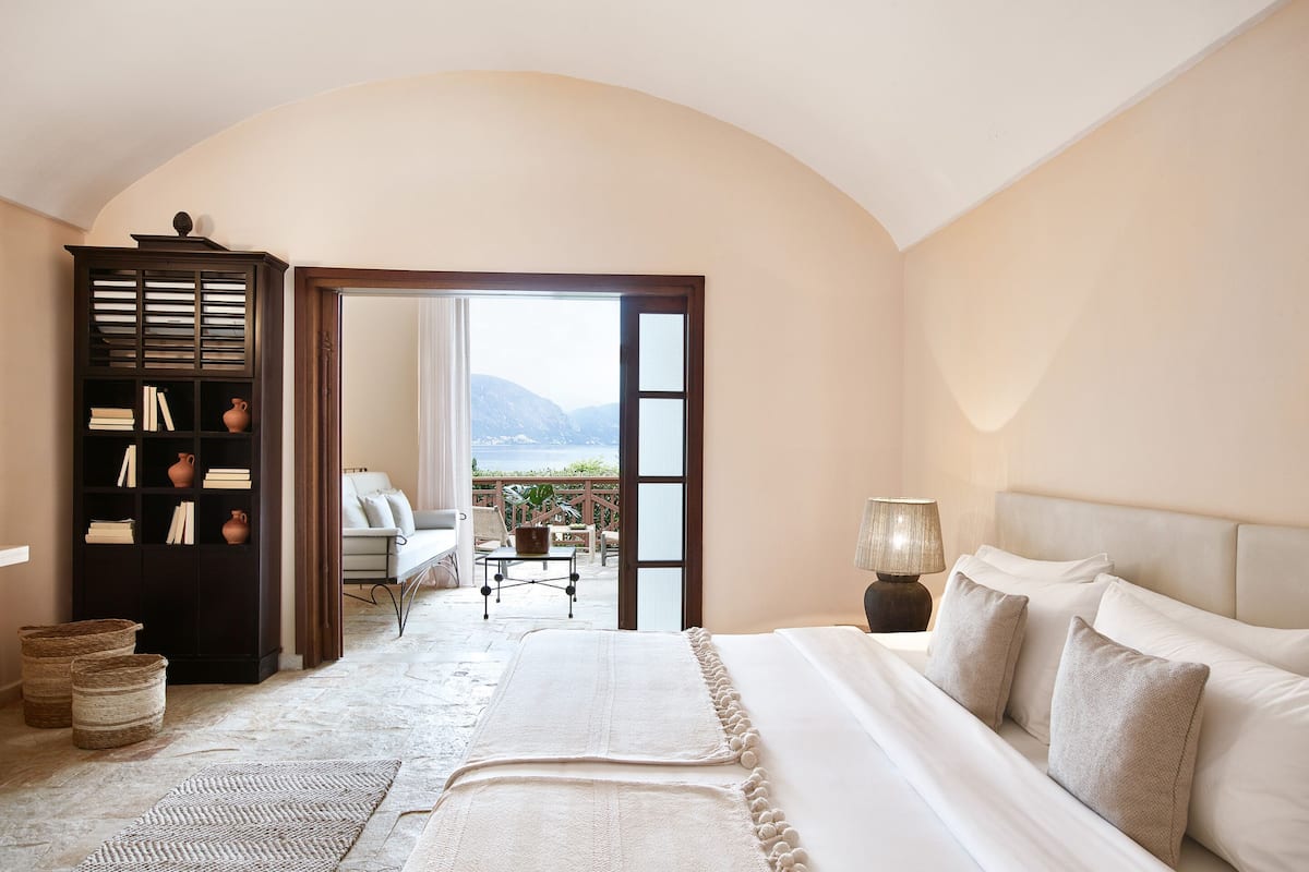 Quarto com cama grande, estante, mesa e vista para o mar.