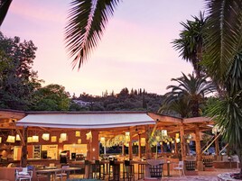 Restaurante ao ar livre com área de estar coberta, vigas de madeira e luzes pendentes.