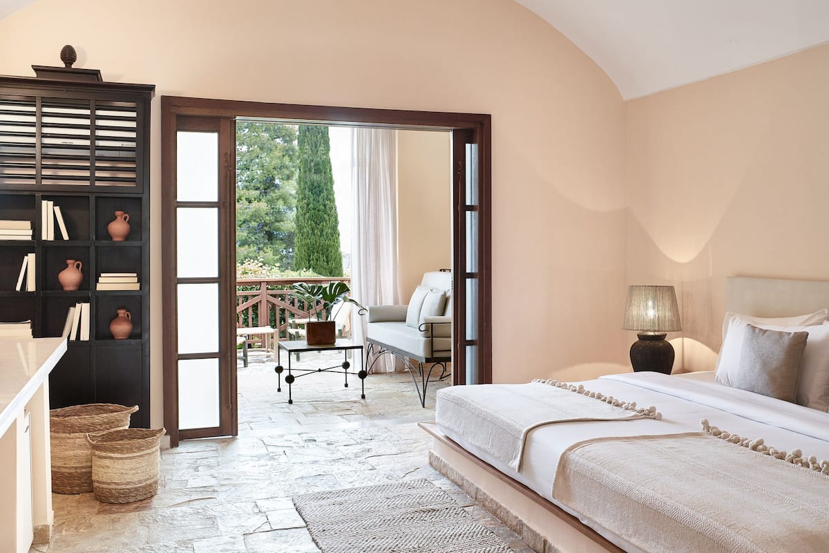 Quarto com uma cama grande, mesa de cabeceira, abajur e vista para o exterior através de uma porta aberta.