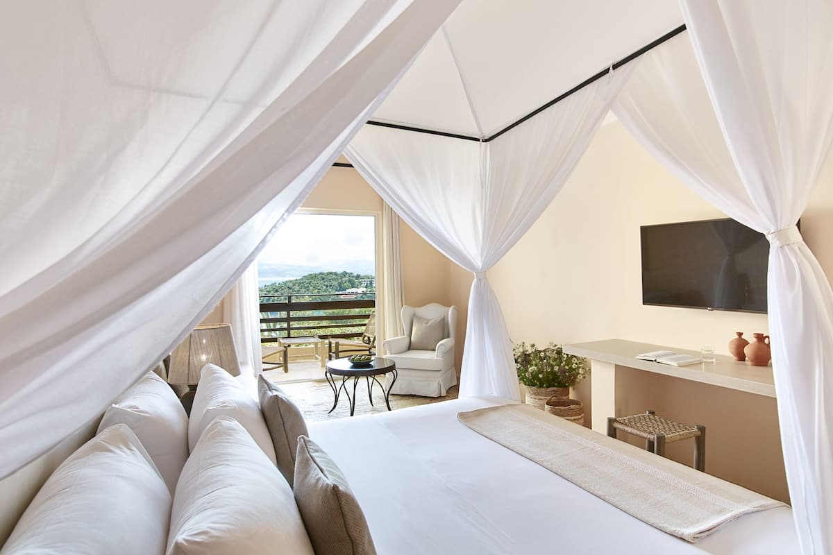 Quarto com cama, escrivaninha, cadeira e varanda com vista.