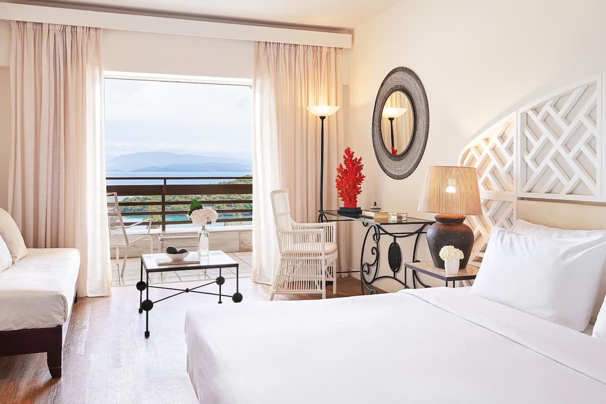 Quarto de hotel com cama, secretária com luminária, cadeira e vista para as montanhas.