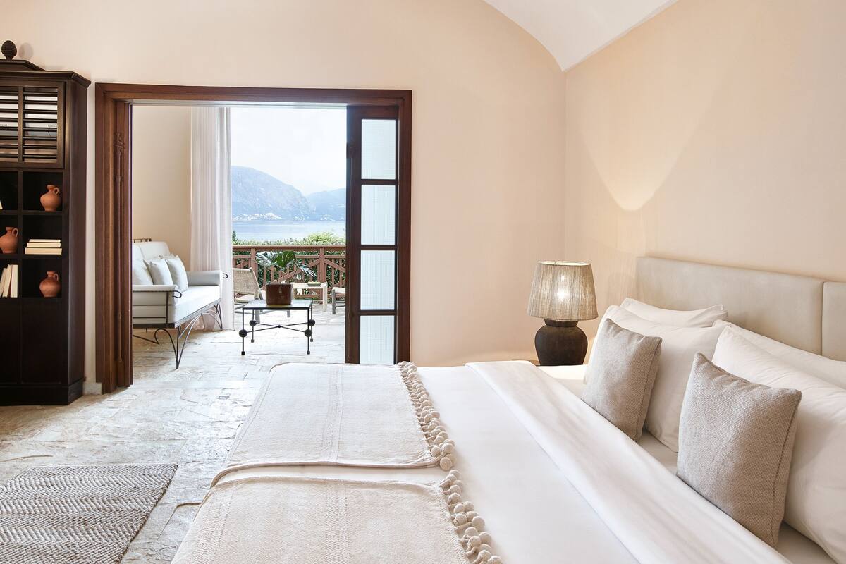 Quarto com cama grande, mesa de cabeceira, luminária e vista para o exterior.