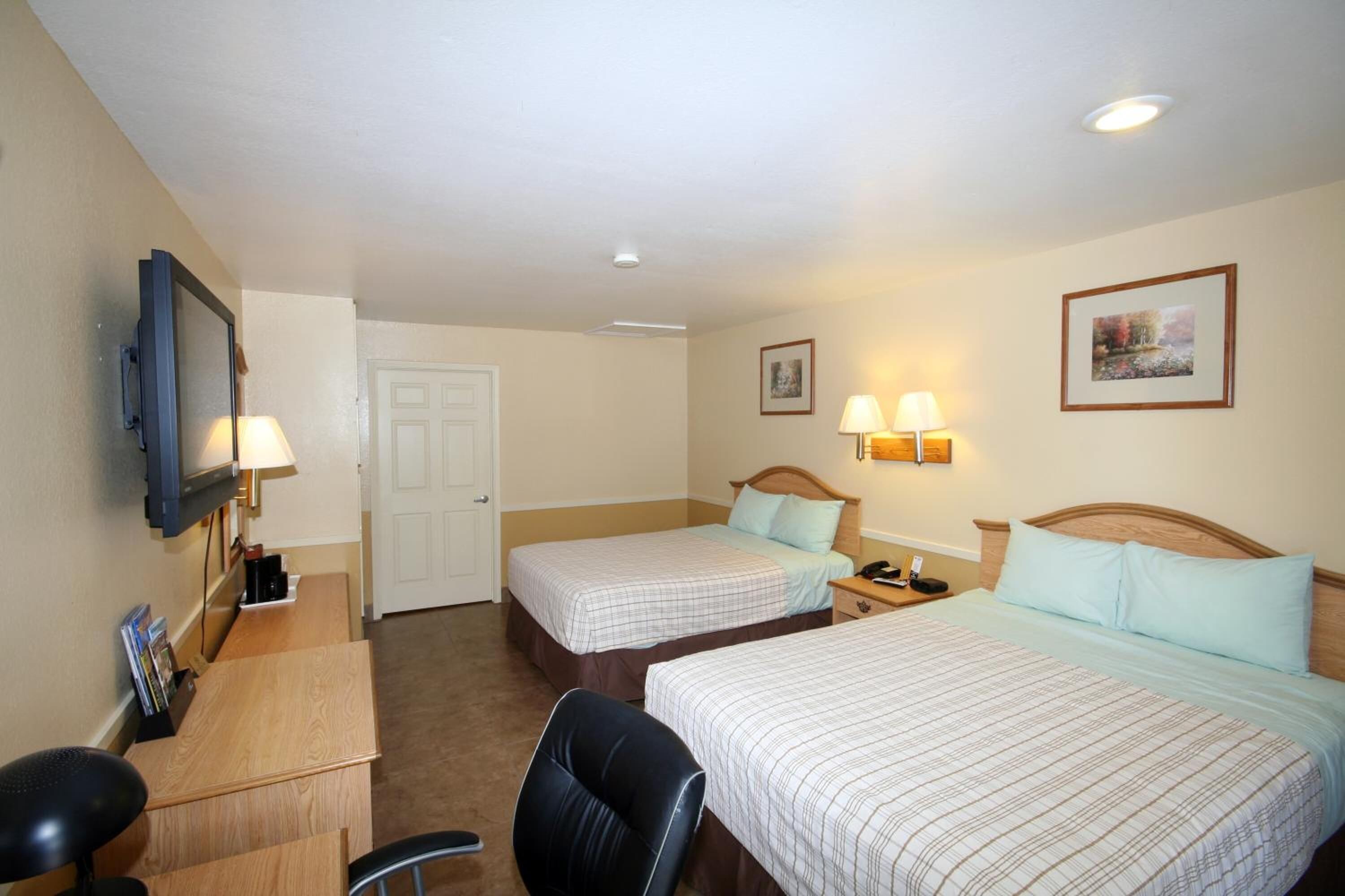 Quarto de hotel com duas camas, uma escrivaninha, uma cadeira, uma televisão e uma porta.