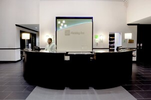 Recepção com uma grande tela exibindo o nome do hotel, um balcão e um homem atrás dele.