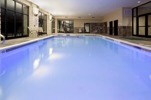 Piscina interna com água cristalina, posto de salva-vidas e área de estar com cadeiras.