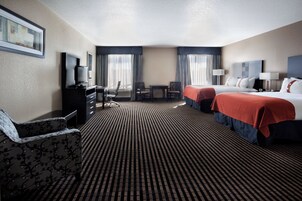 Quarto de hotel com cama, escrivaninha, cadeira, televisão e janela com cortinas.