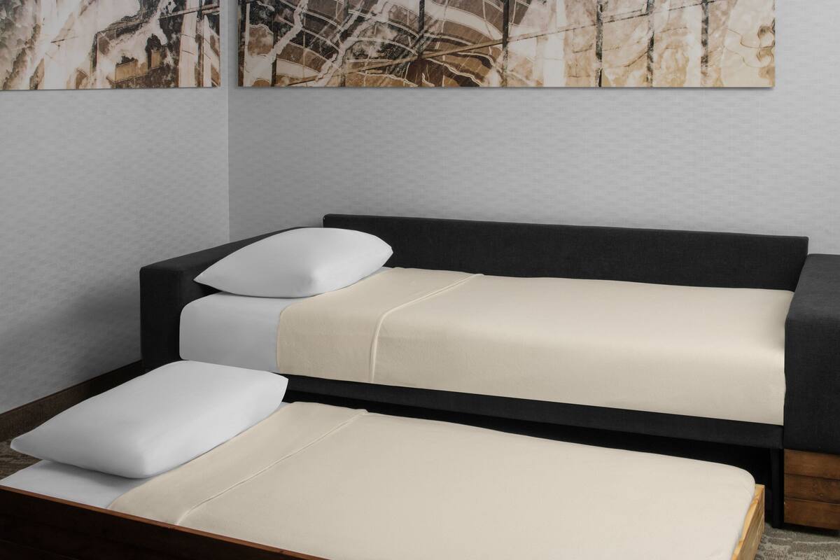 Um quarto moderno com uma cama, um banquinho e uma obra de arte na parede.
