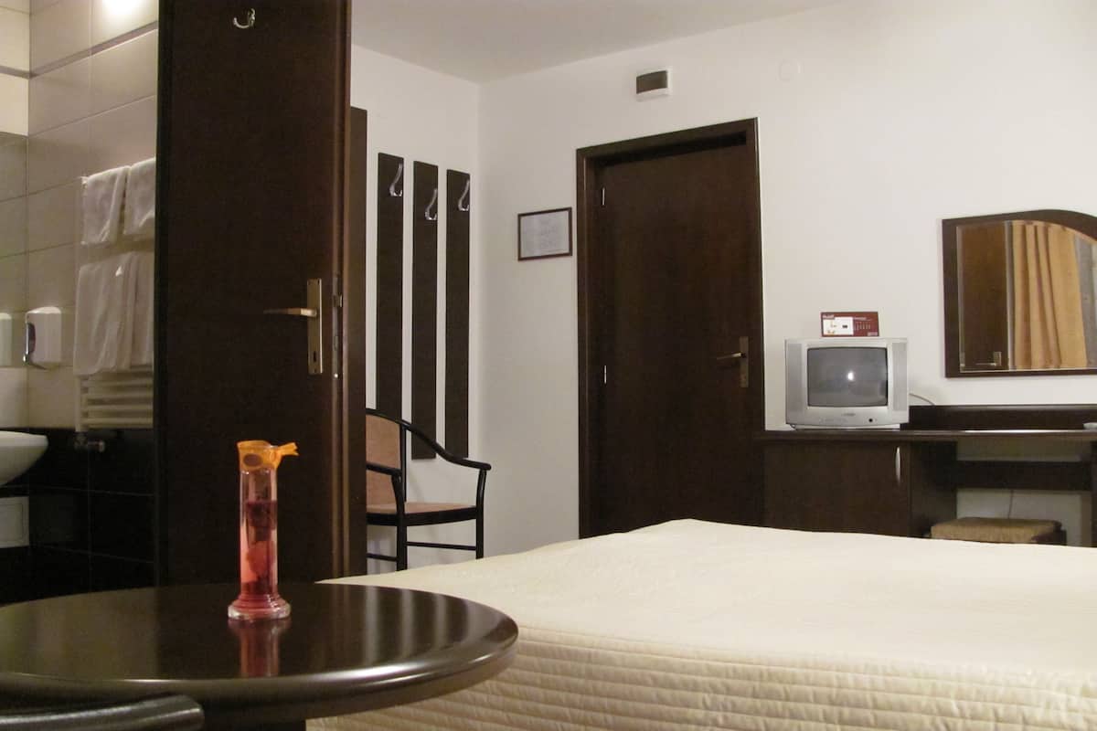 Quarto de hotel com cama, uma mesinha, uma cadeira, televisão e banheiro com pia e porta-toalhas.
