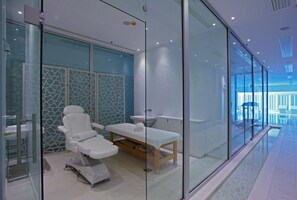 Uma sala de spa moderna com mesa de massagem, divisória de vidro e vista para uma varanda.