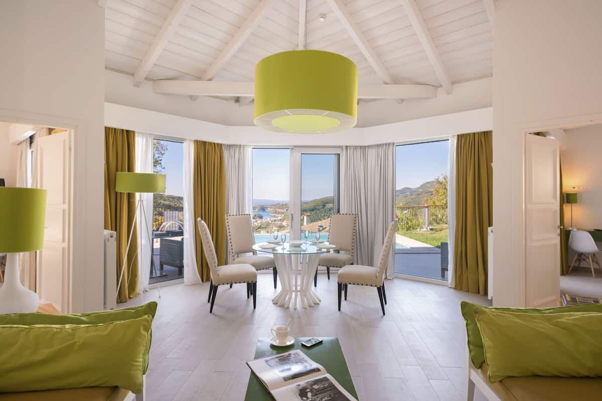 Um quarto espaçoso com mesa e cadeiras de jantar, janelas amplas com cortinas e vista para a paisagem.