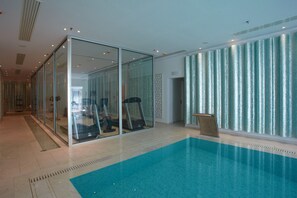 Piscina interna moderna com paredes de vidro, esteira e uma grande janela com cortinas.
