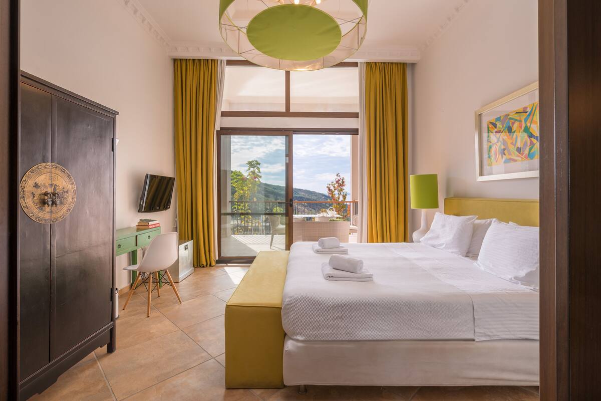 Quarto de hotel com cama, escrivaninha, cadeira, guarda-roupa e varanda com vista.