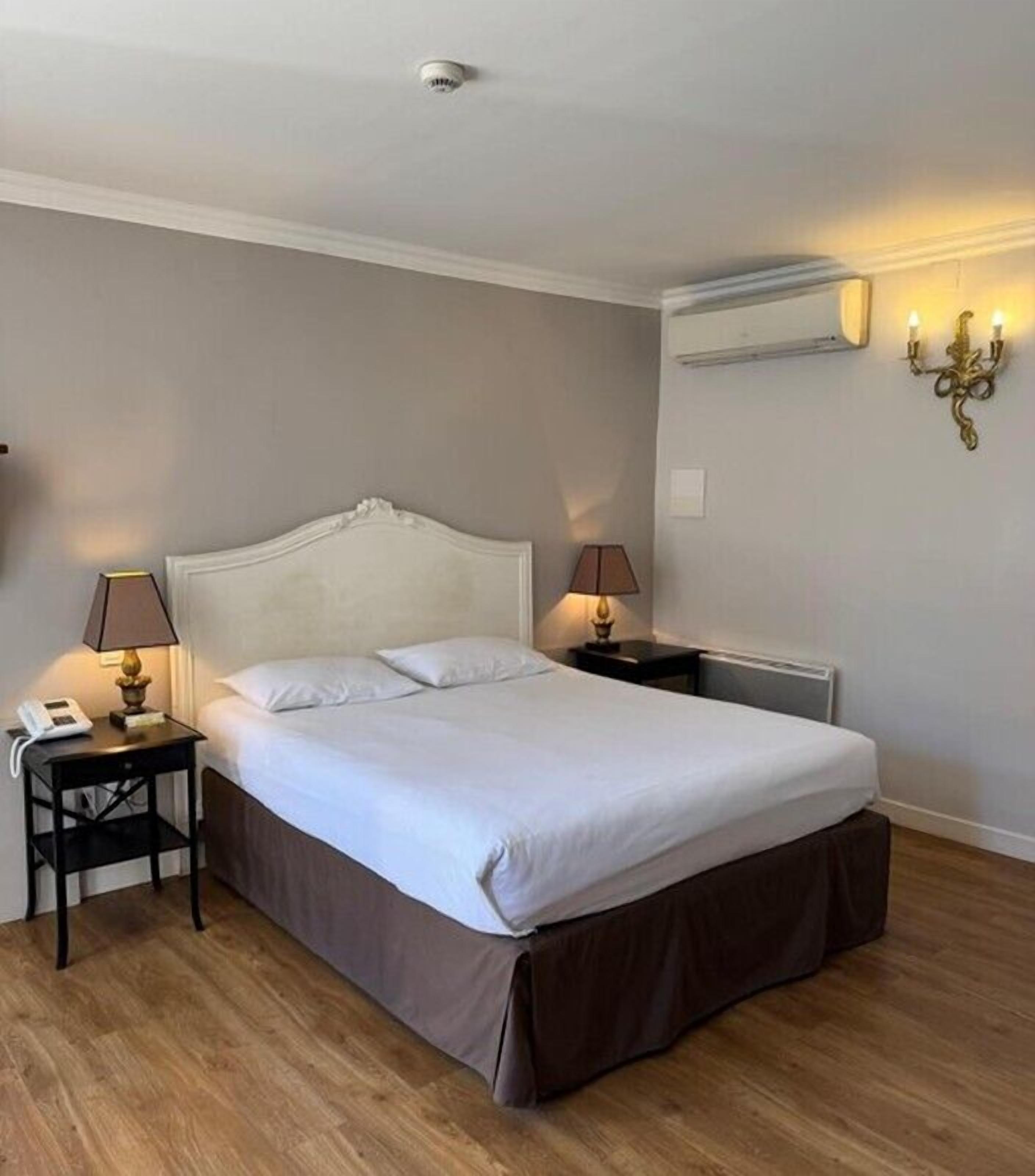 Quarto de hotel com uma cama grande, duas mesas de cabeceira com abajures, um ar condicionado e um candeeiro fixado na parede.