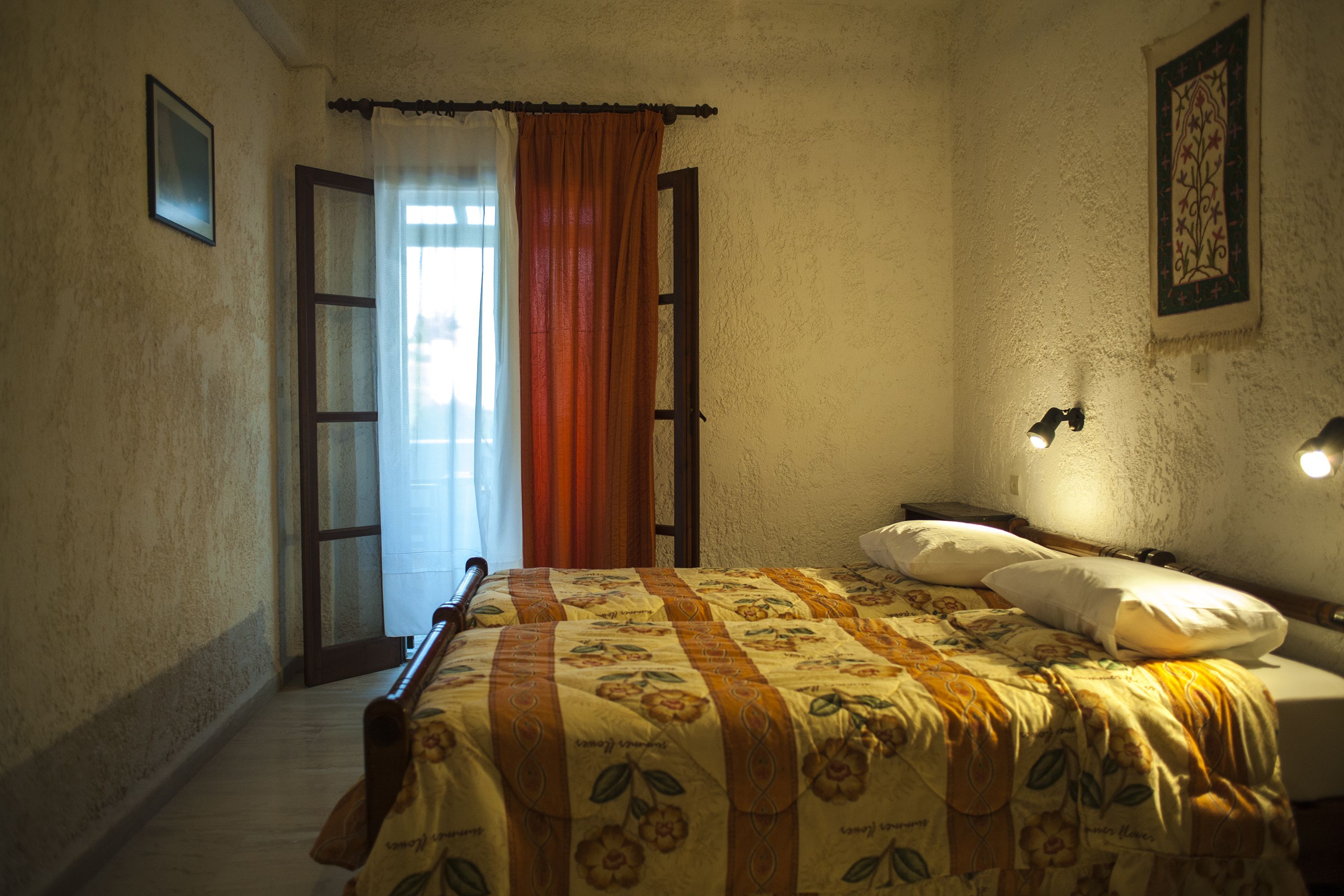 Quarto com cama, mesa de cabeceira, luminária na parede e porta com cortinas.