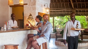 Uma área de bar com parede de pedra, banquetas de madeira e alguém servindo bebidas.