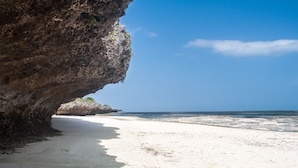 Uma praia com uma grande formação rochosa e céu azul límpido.