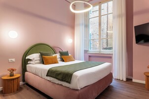 Quarto com cabeceira verde, roupa de cama branca e janela com cortinas brancas.
