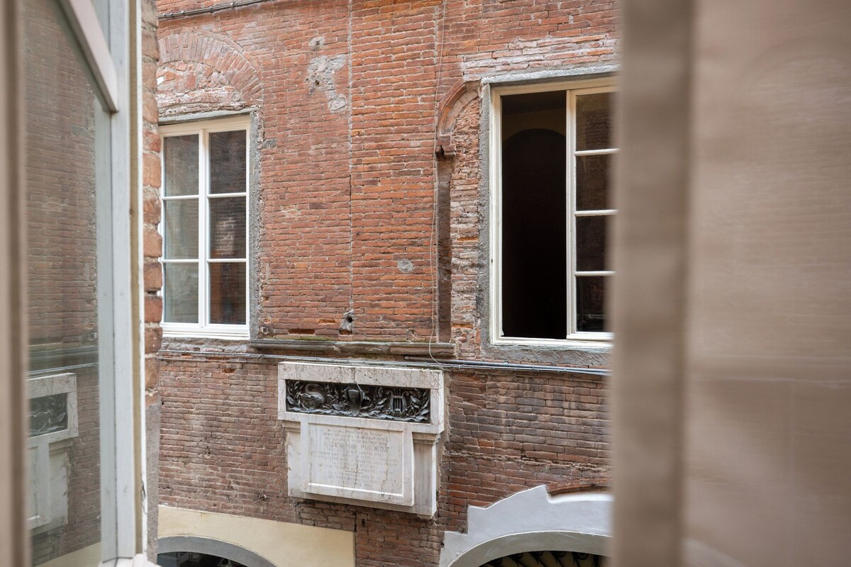 Uma viela estreita com um edifício de tijolos, com duas janelas, uma delas tapiada.