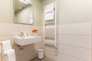 Casa de banho com lavatório branco, espelho, suporte para toalhas e uma toalha branca.