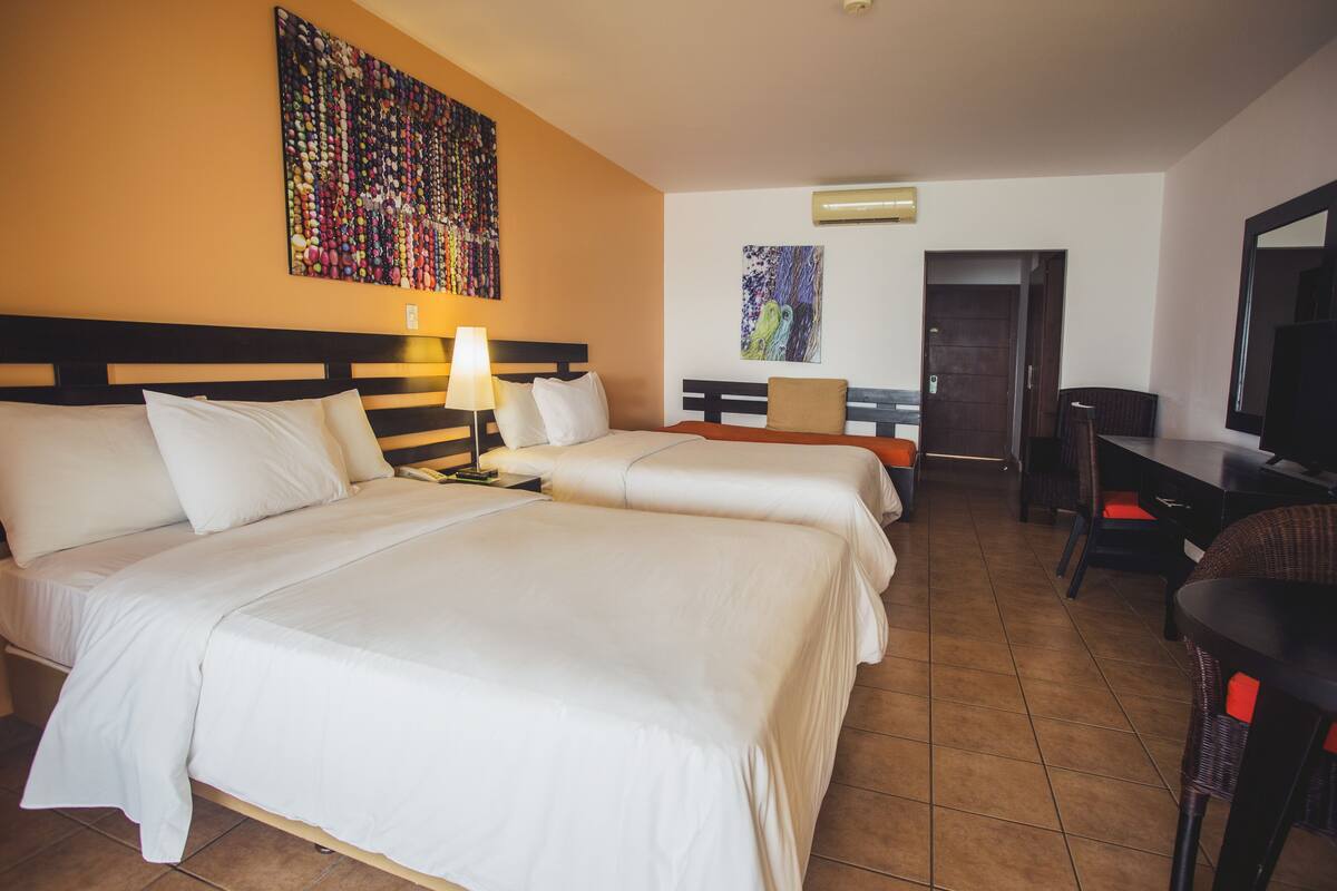 Quarto de hotel com duas camas, uma escrivaninha, uma cadeira e obras de arte nas paredes.