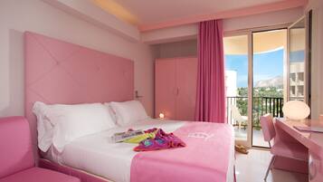 Quarto de hotel em tons de rosa, com cama, escrivaninha, cadeira e varanda com vista.