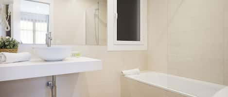 Uma casa de banho moderna com lavatório branco, um espelho grande, cabine de duche em vidro e uma banheira branca.