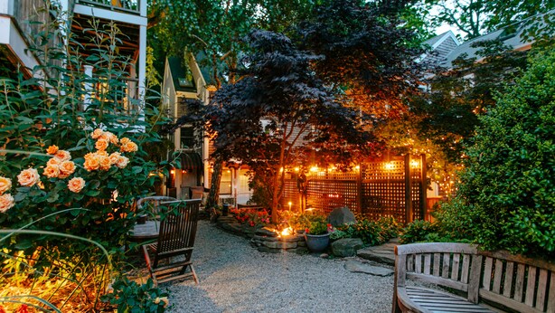 Um jardim com um banco de madeira, uma lareira e uma pérgola com luzes de cordão.