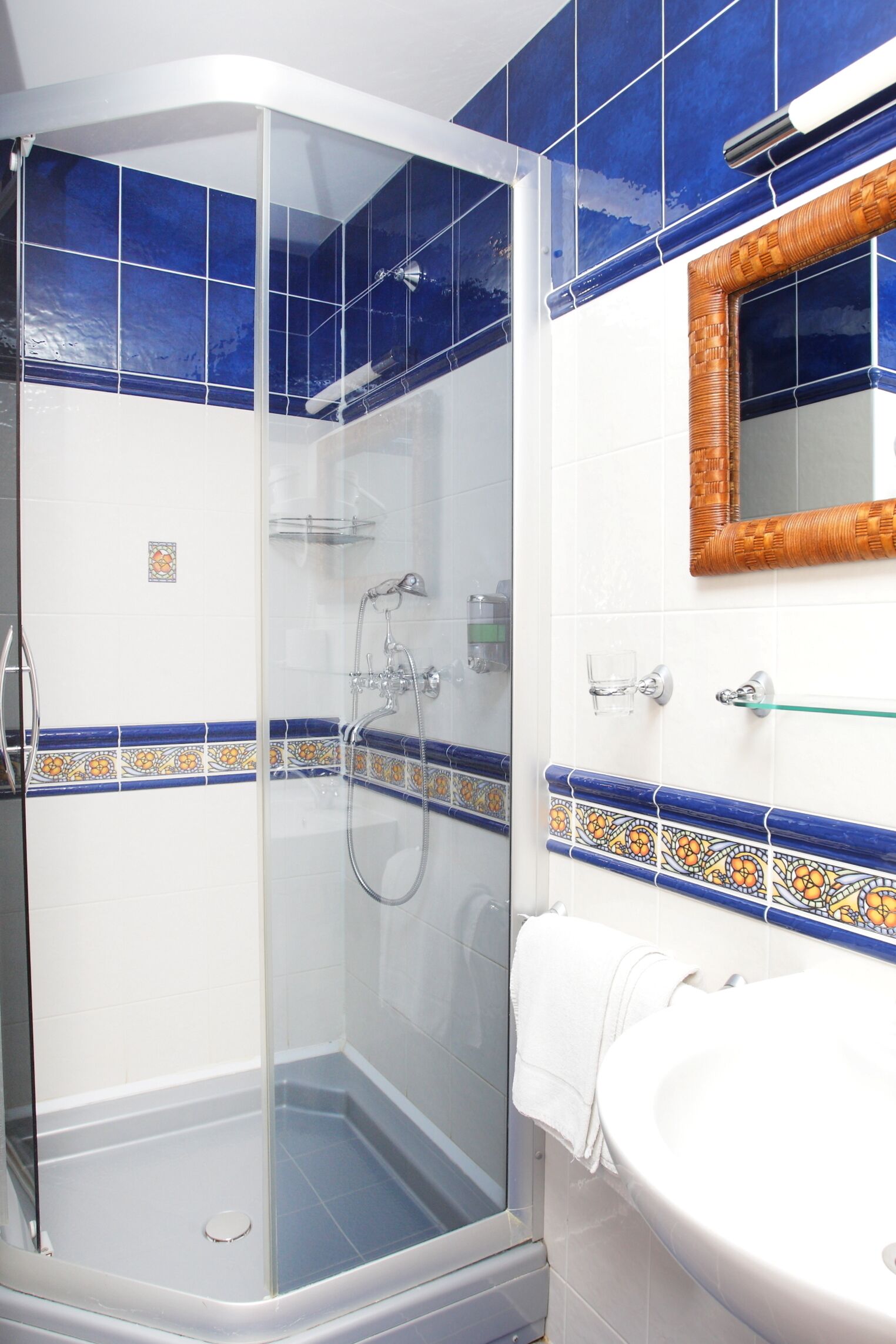 Casa de banho com chuveiro envidraçado, lavatório branco e paredes com azulejos azuis.