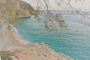 Paisagem costeira com costa rochosa, águas turquesa cristalinas e vegetação rala.