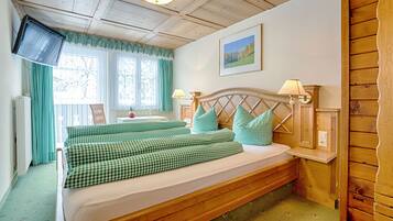 Uma cama de madeira com roupa de cama xadrez, uma televisão fixada na parede e uma janela com cortinas.