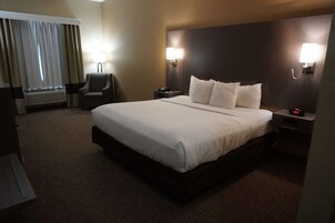 Quarto de hotel com uma cama grande, duas mesas de cabeceira, uma cadeira, uma escrivaninha e um abajur.