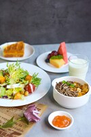 Uma mesa com diversos pratos, incluindo uma salada, frutas, uma tigela de cereais e um copo de leite.