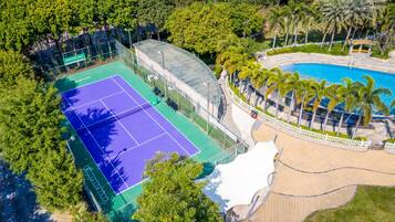 Vista aérea de uma quadra de tênis cercada por palmeiras e uma piscina.