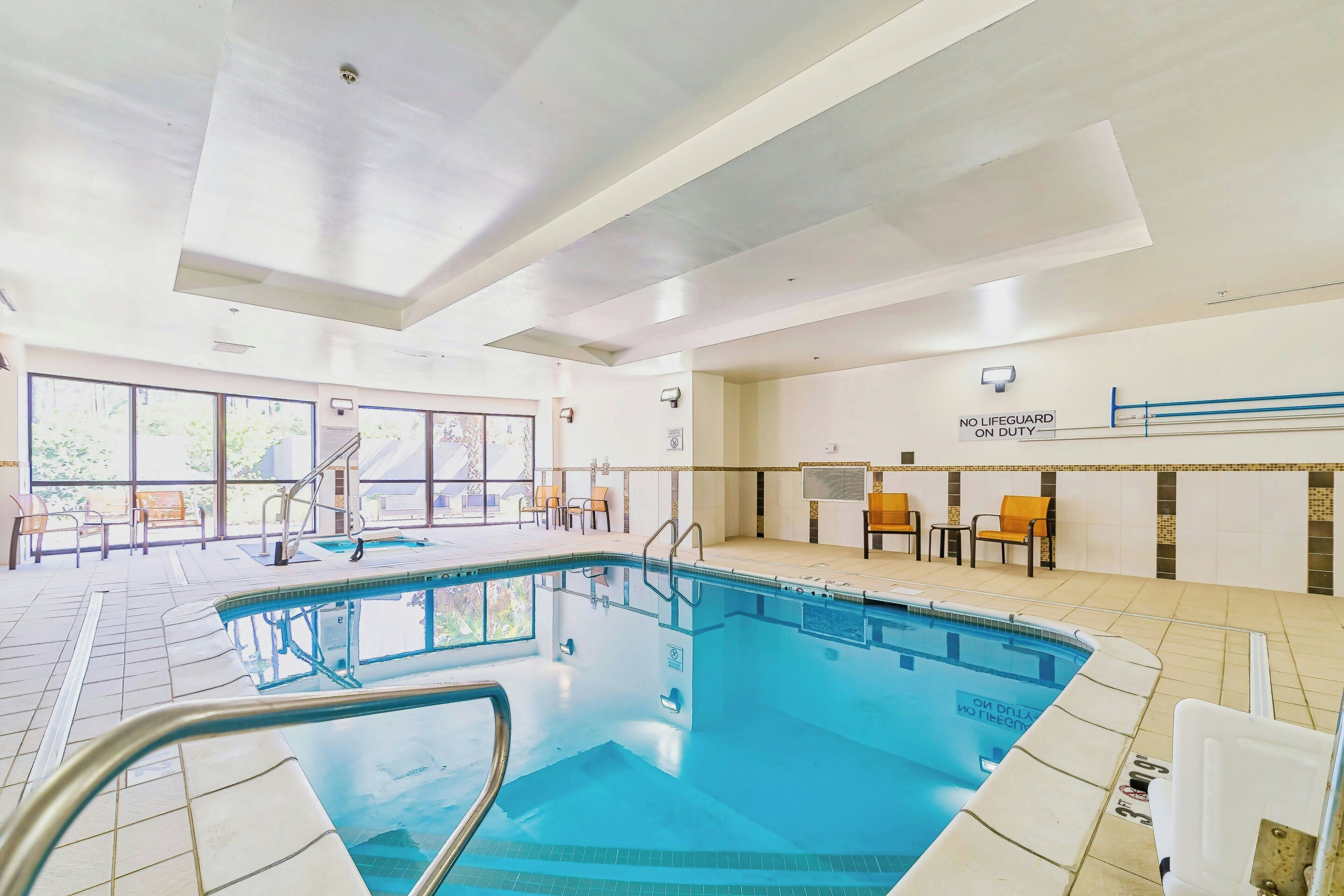 Piscina interior com água azul cristalina, rodeada por pavimento ladrilhado e equipada com grades de segurança.