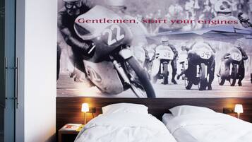 Quarto com um mural grande na parede retratando uma corrida de motocicletas antigas, uma cama, abajures e uma cabeceira de madeira.