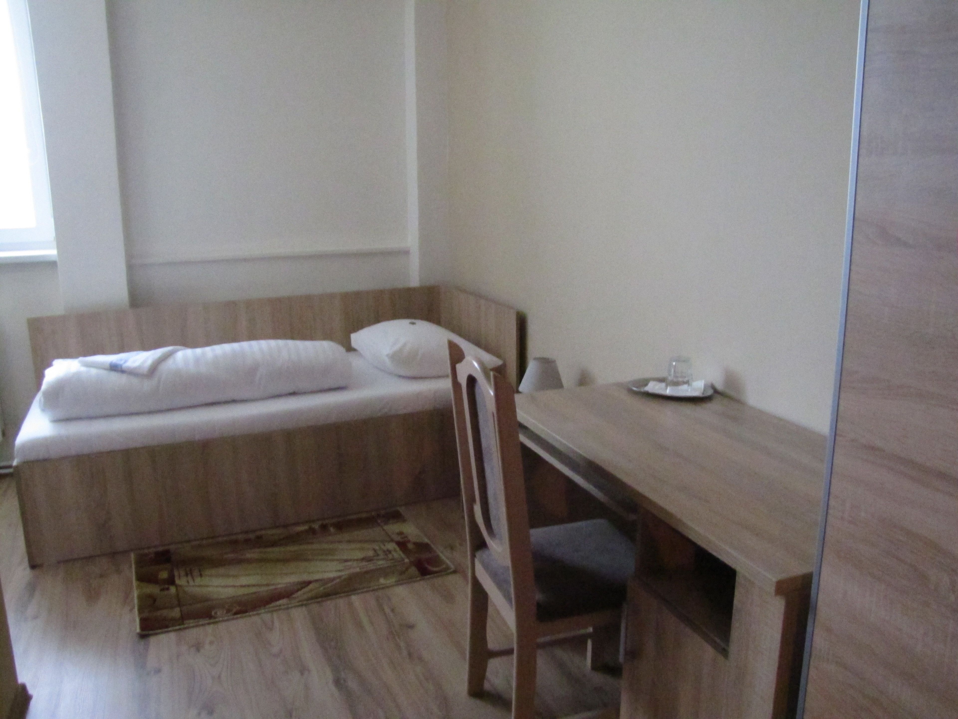 Quarto pequeno e funcional com cama, escrivaninha e cadeira.