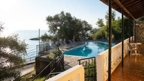 Uma área de piscina com vista para o mar, cadeiras de descanso e um espaço de estar coberto.
